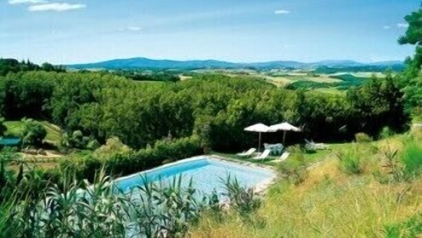 Área de piscina cercada por vegetação exuberante e colinas ao fundo.