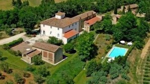 Vista aérea de uma grande propriedade com vários edifícios, piscina e vegetação ao redor.