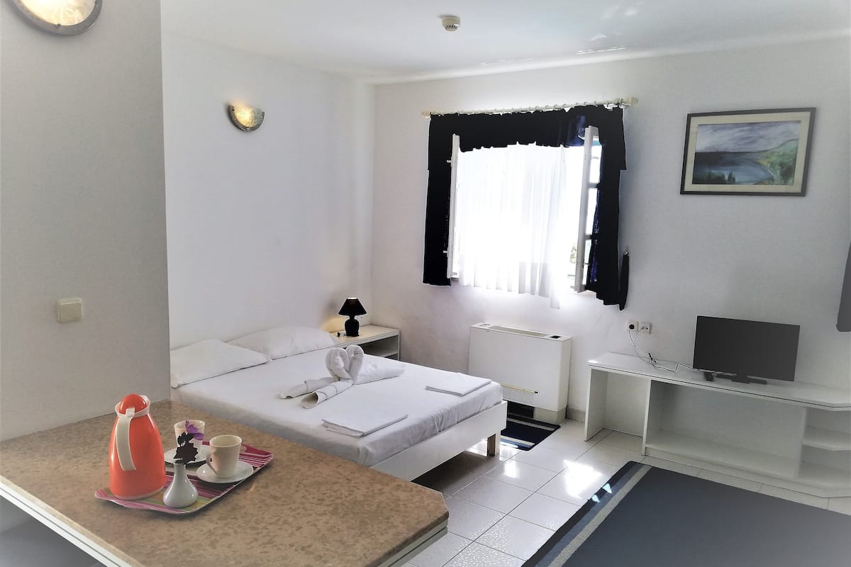 Quarto de hotel com cama, mesa de cabeceira, luminária, TV e um quadro na parede.