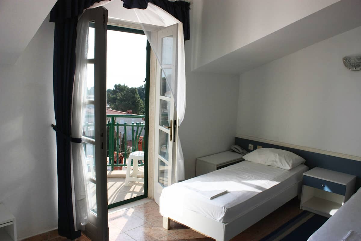 Quarto com cama, mesa de cabeceira, janela com cortinas e vista para o exterior.