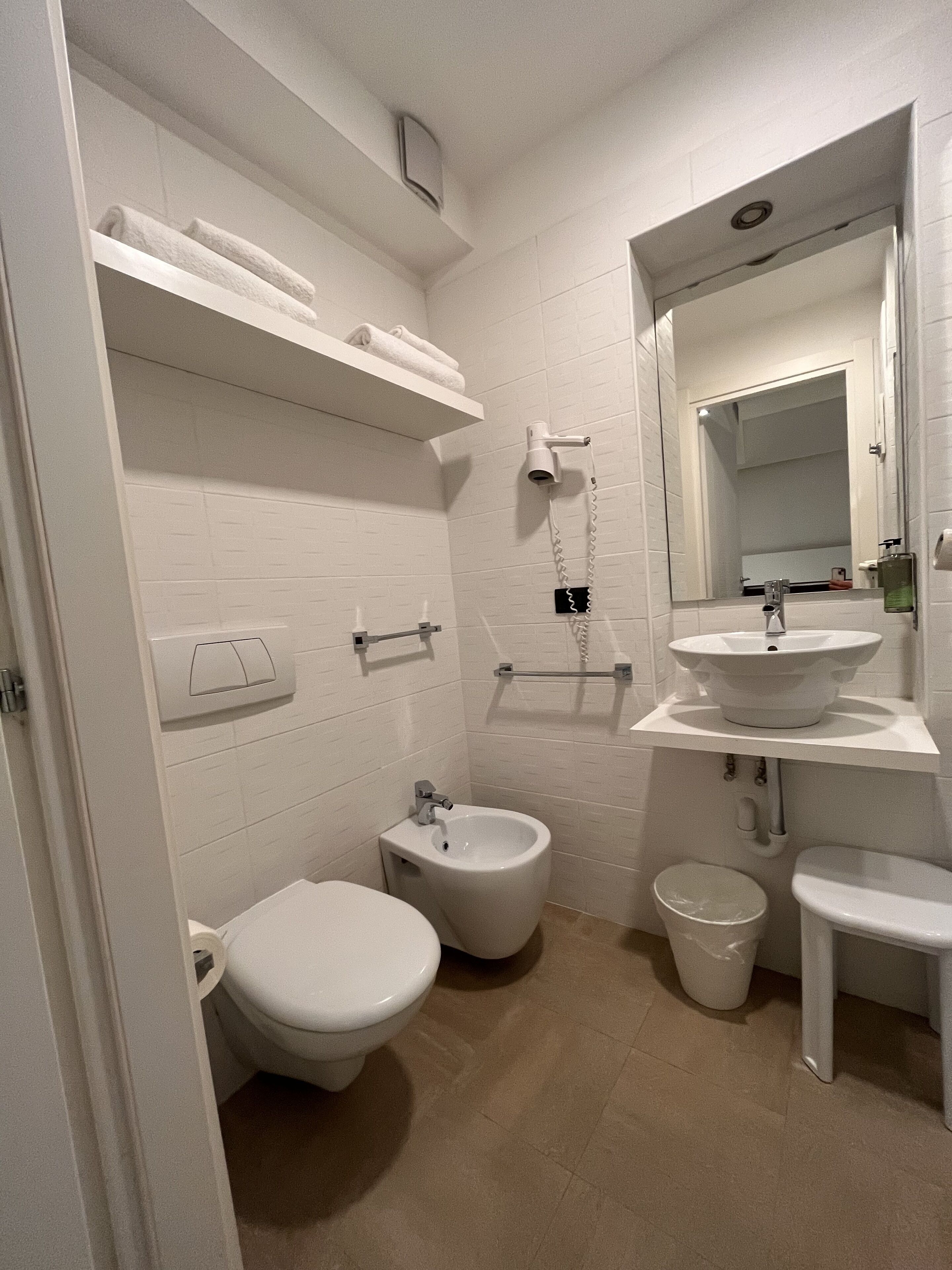 Uma casa de banho moderna com sanita, bidé, lavatório e suporte para toalhas.