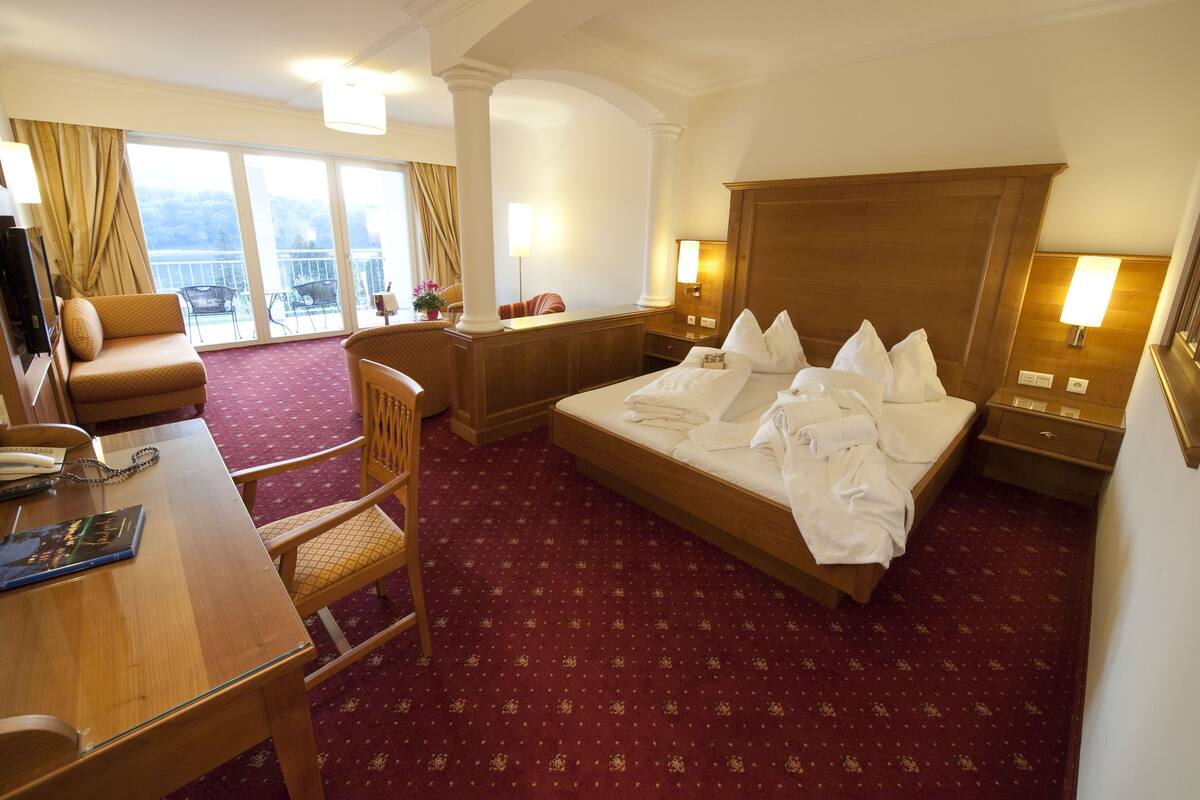 Quarto de hotel com uma cama grande, uma mesa, uma cadeira, um sofá e varanda com vista.