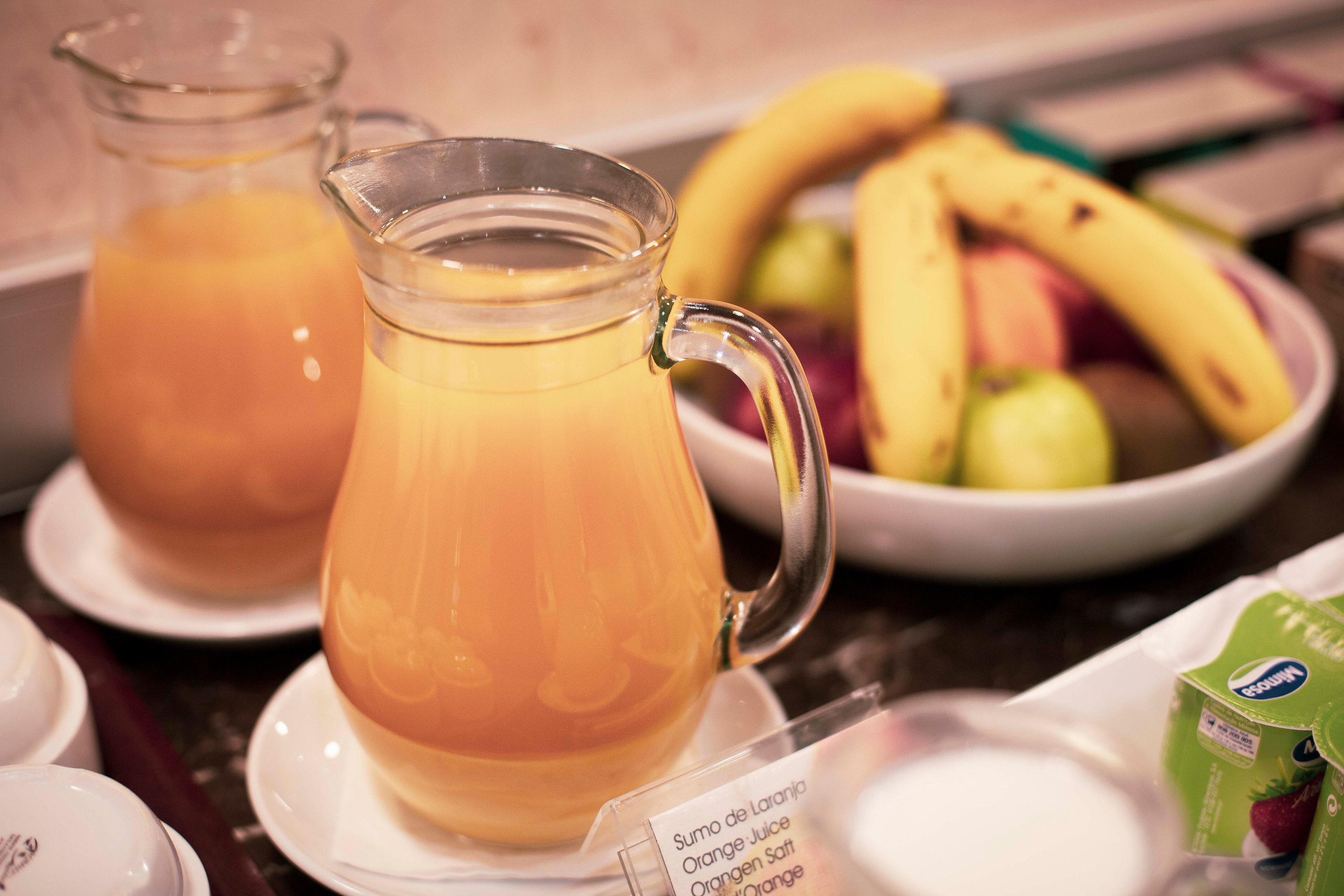 Uma jarra de sumo de laranja e uma travessa de fruta sobre uma mesa.