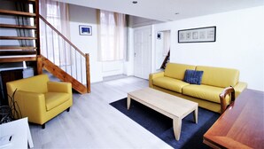 Uma sala de estar com um sofá amarelo, uma mesa de centro de madeira e uma escada.