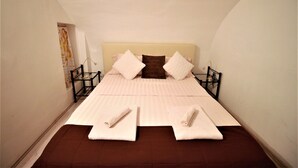 Cama bem arrumada com roupa de cama branca e marrom, dois travesseiros e duas toalhas enroladas.