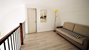 Um corredor com corrimão de madeira, um sofá bege, um quadro e um abajur.