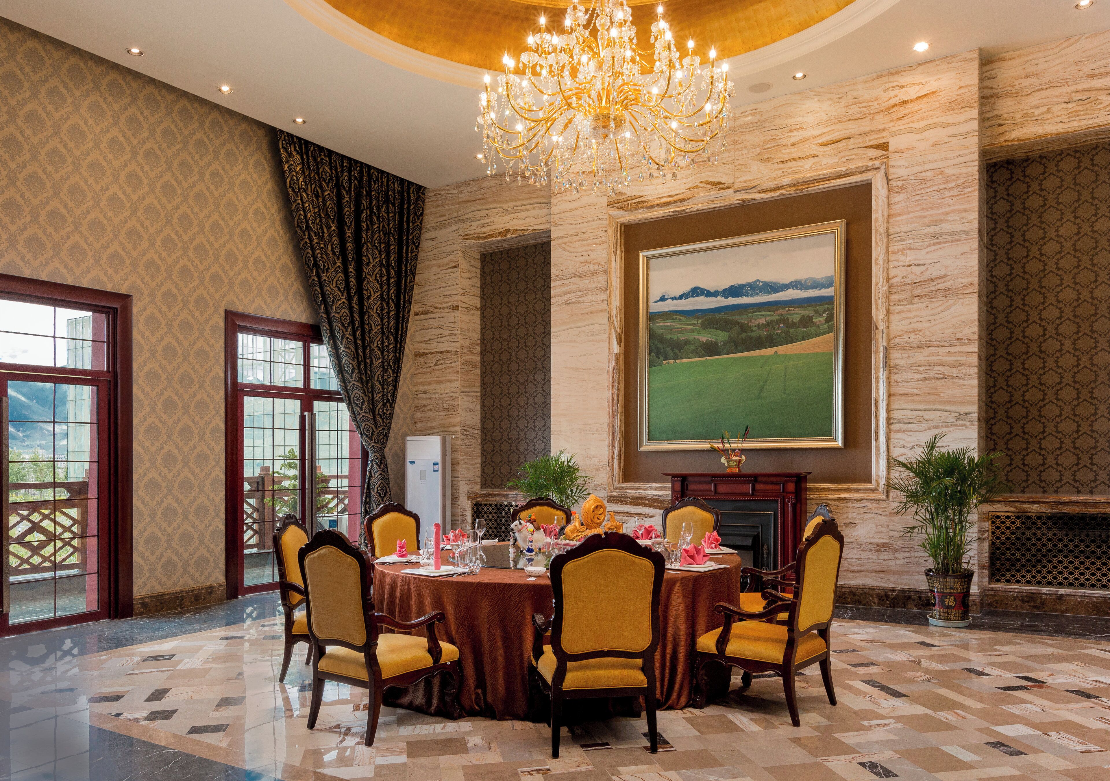 Uma sala de jantar formal com um candelabro, uma lareira e um grande quadro paisagístico na parede.