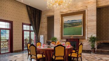 Uma sala de jantar formal com um candelabro, uma lareira e um grande quadro paisagístico na parede.