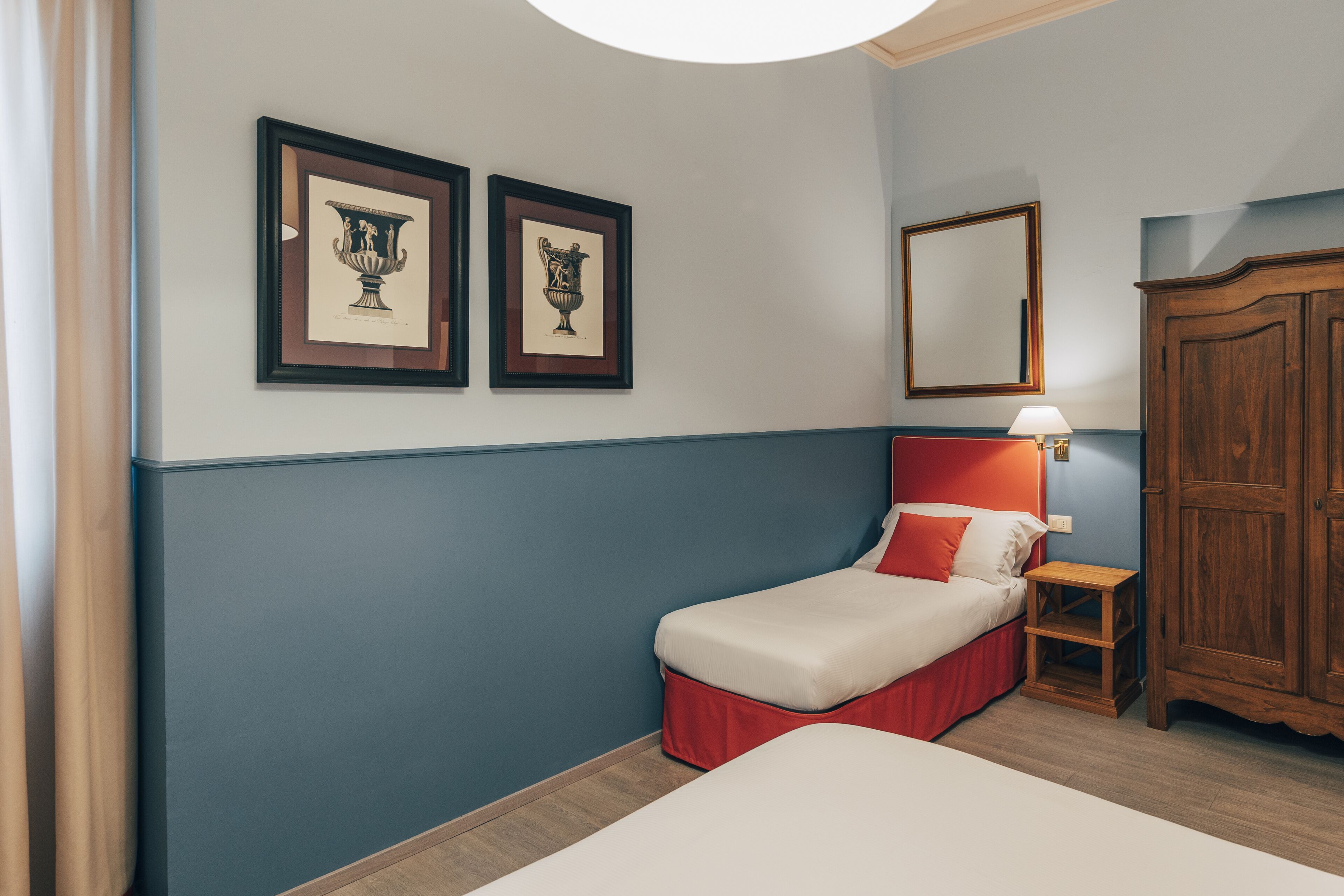 Um quarto com cama, mesa de cabeceira, guarda-roupa de madeira e duas imagens emolduradas na parede.