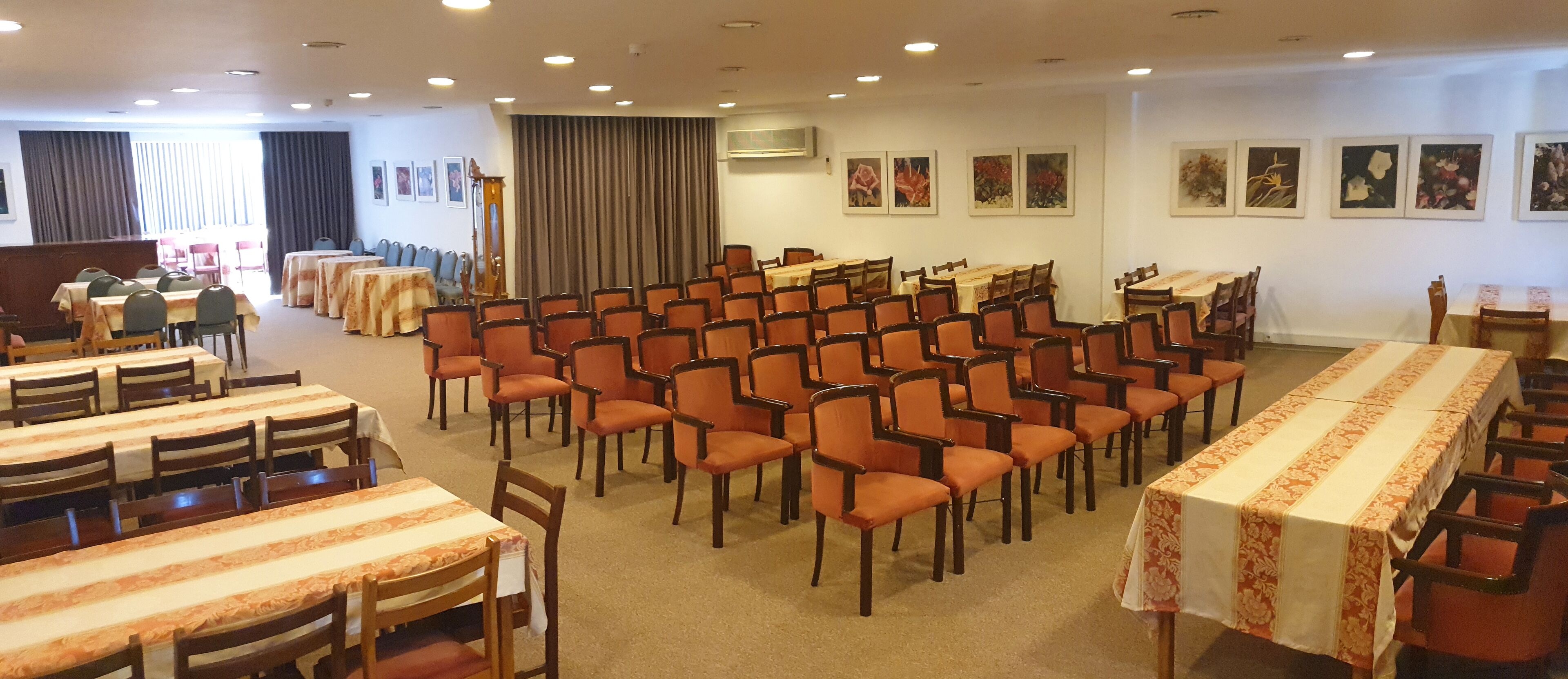 Uma sala de conferência com fileiras de cadeiras e mesas laranja, um púlpito e quadros nas paredes.