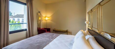 Quarto de hotel com cama, mesa de cabeceira, luminária, janela com cortinas e vista para edifícios.