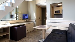 Quarto de hotel moderno com escrivaninha, TV de tela plana, sofá e micro-ondas.