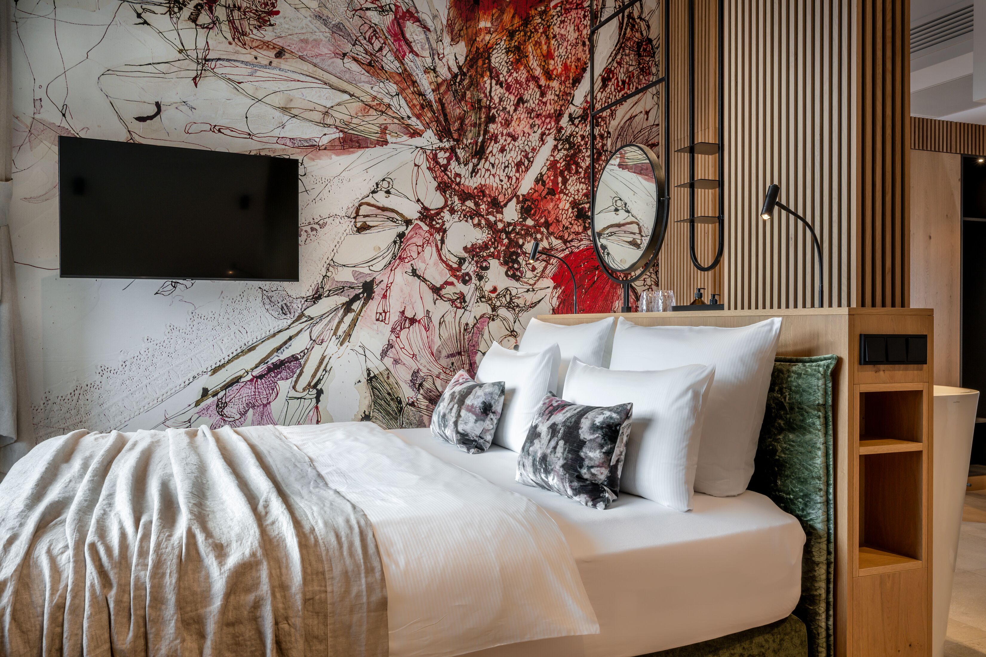 Um quarto moderno com uma cama grande, uma televisão montada e uma arte floral única na parede.