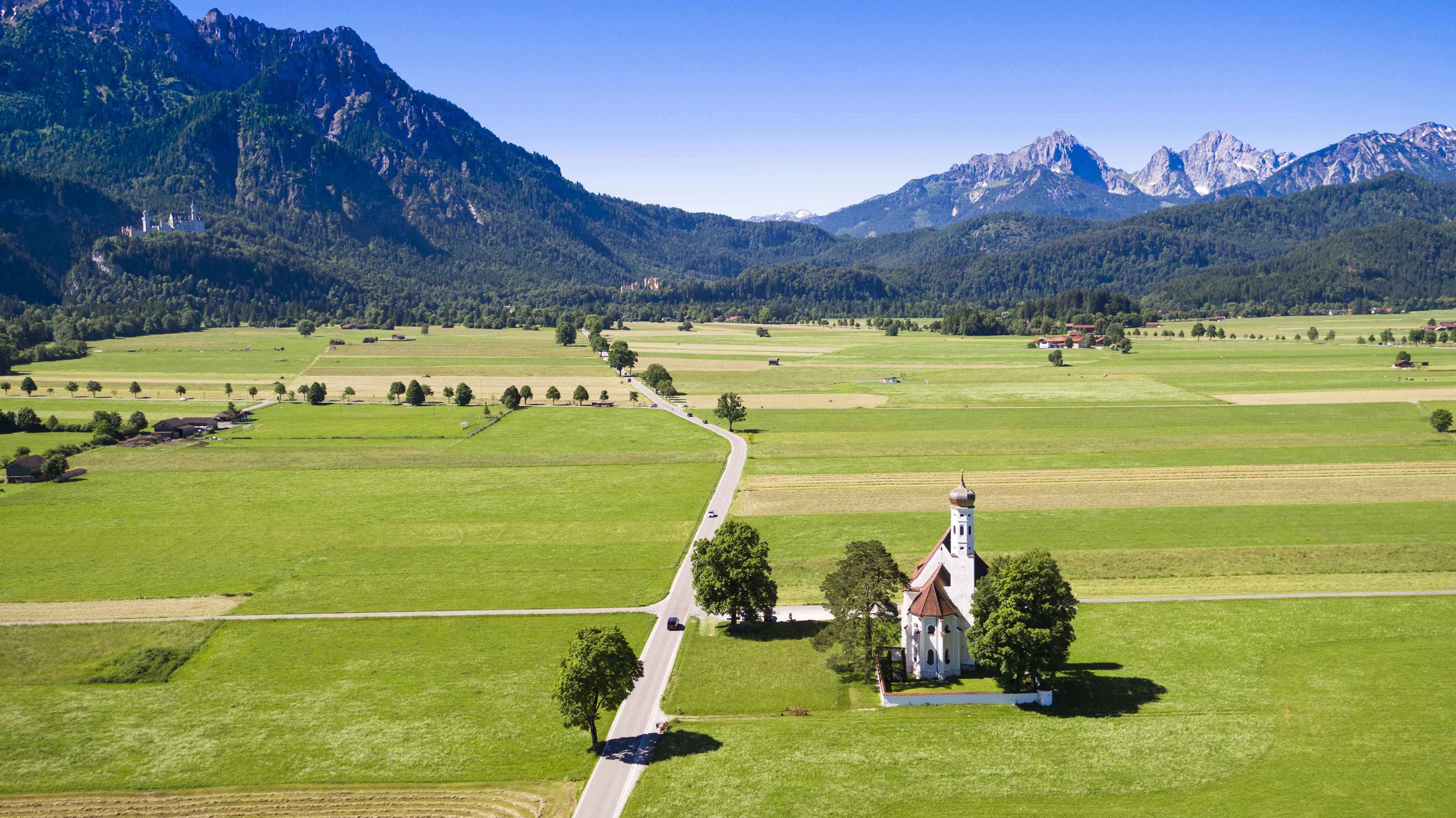 Paisagem rural com uma igreja, campos e montanhas.
