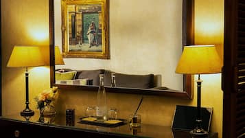 Quarto de hotel com espelho, duas luminárias, um vaso com flores, um tabuleiro com copos e um quadro na parede.