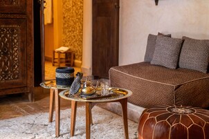 Um quarto aconchegante com sofá, bandeja decorativa com bule e xícaras, e um banquinho estampado.