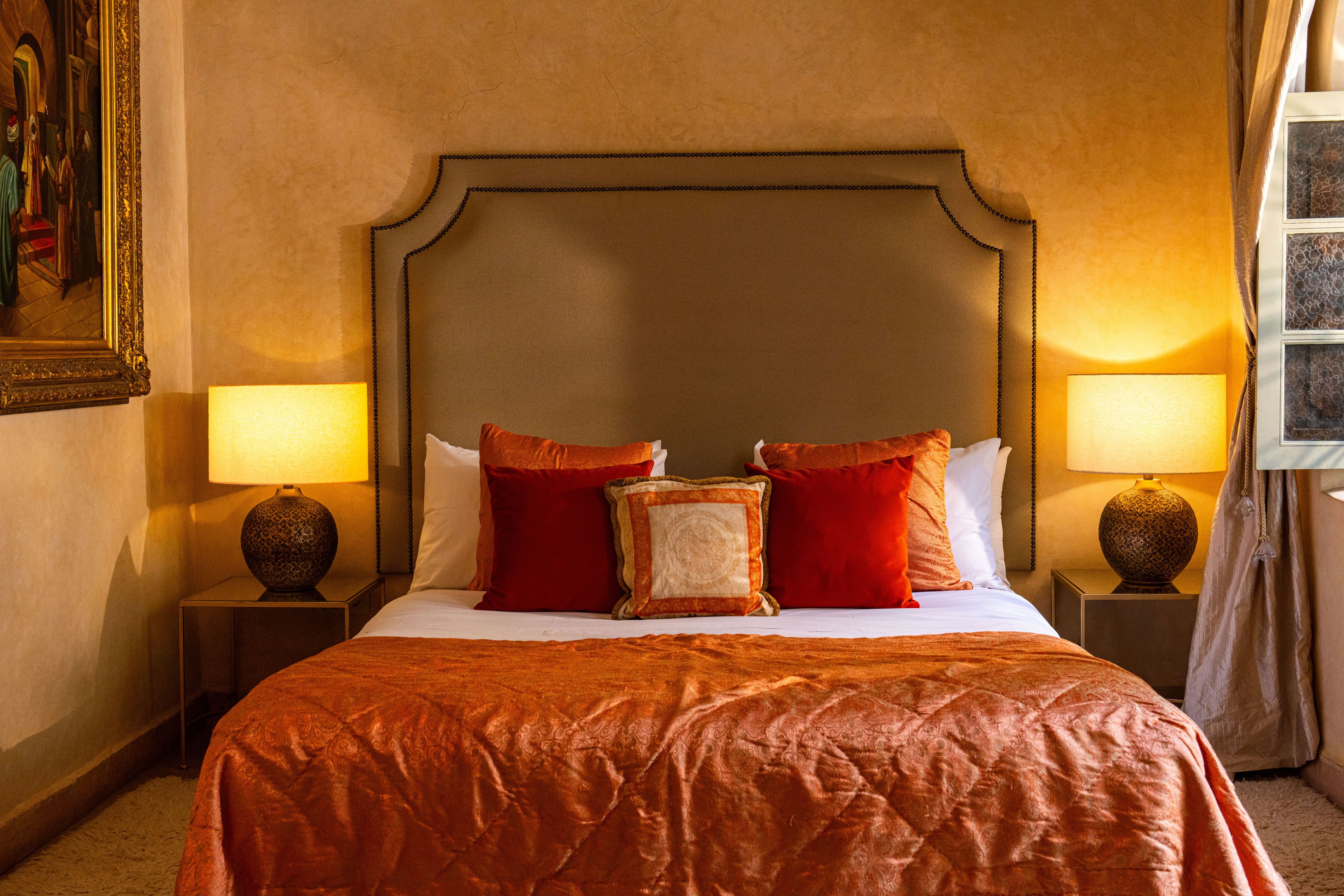 Quarto de hotel com uma cama grande, duas luminárias de cabeceira, um quadro na parede e uma janela com cortinas.