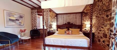 Quarto com cama de dossel, piso de madeira, paredes de pedra e um candelabro.
