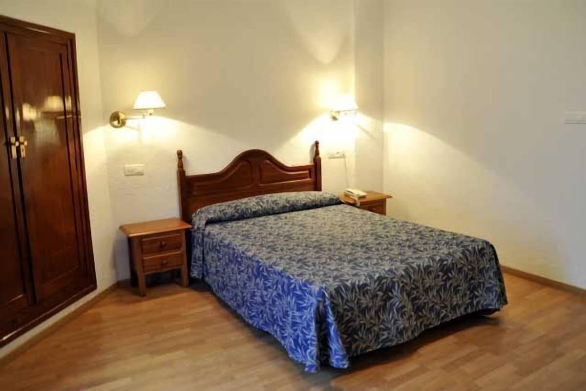 Quarto com cama de madeira, duas luminárias de cabeceira, mesa de cabeceira e guarda-roupa de madeira.