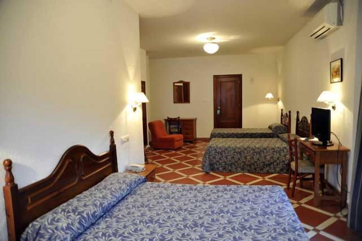 Quarto de hotel com duas camas, uma escrivaninha, uma cadeira e uma televisão.