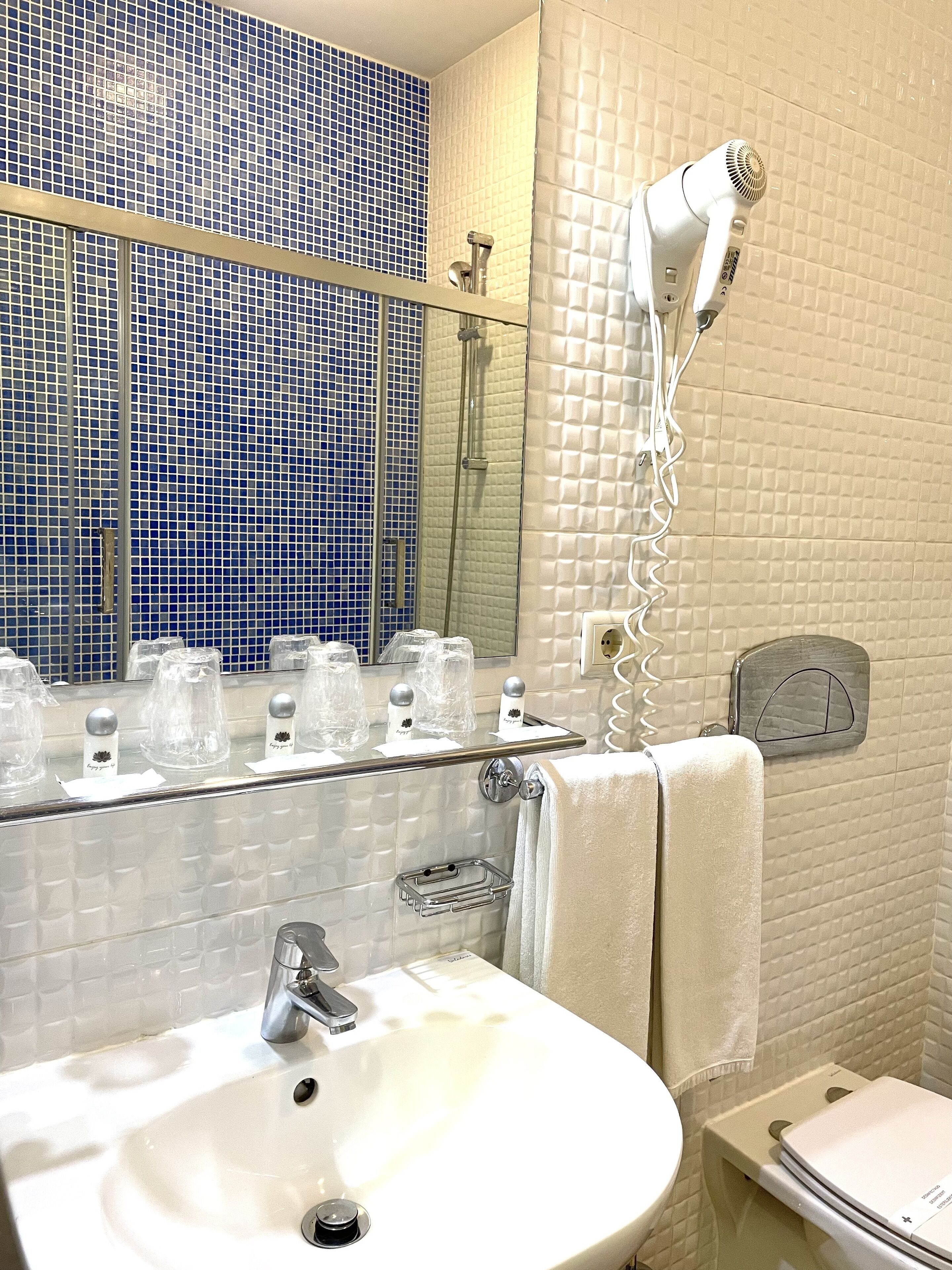 Casa de banho com lavatório, espelho e secador de cabelo fixado na parede.