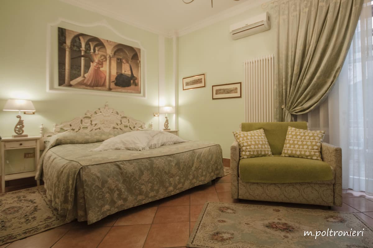 Um quarto com cama, sofá verde, lustre e um quadro na parede.