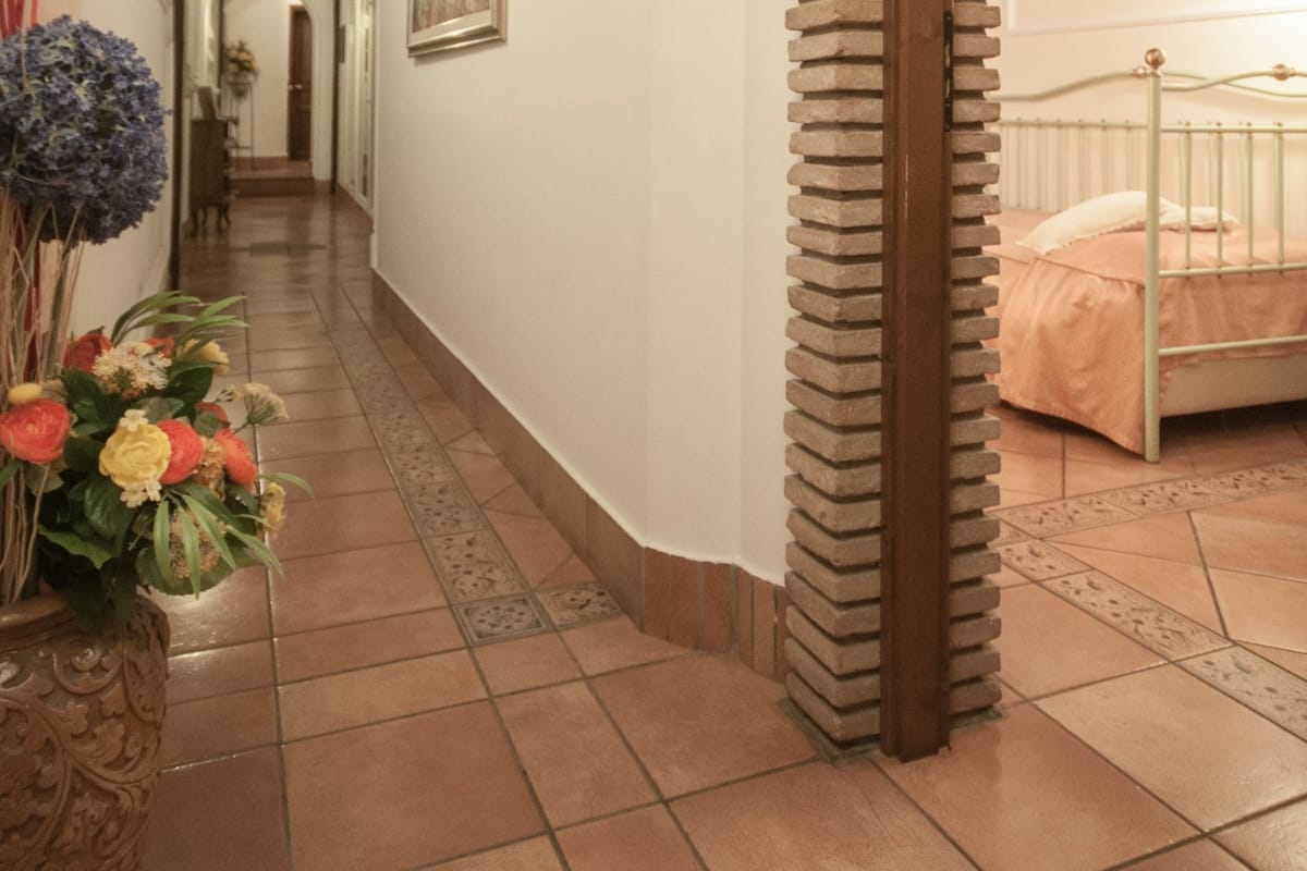Um corredor com chão de azulejos, teto de madeira e uma cama com estrutura de metal no quarto.