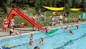 Piscina com um escorrega vermelho e pessoas nadando e brincando.
