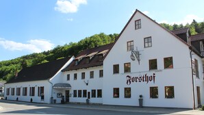 A white building with the name "Forsthof" on its facade, featuring multiple windows and a sloped roof.