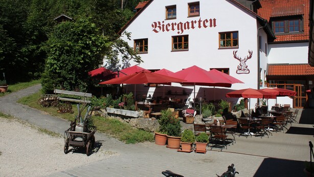 Um edifício com o nome "Biergarten" e área externa com mesas e guarda-sóis vermelhos.