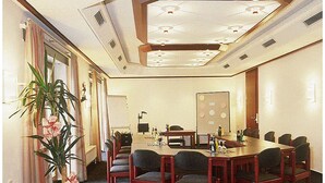 Uma sala de conferências com uma mesa grande, várias cadeiras e um vaso de planta.