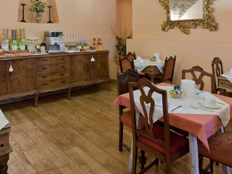 Uma área de refeições com mesas e cadeiras de madeira, um balcão de buffet com comida e bebidas, e um espelho na parede.