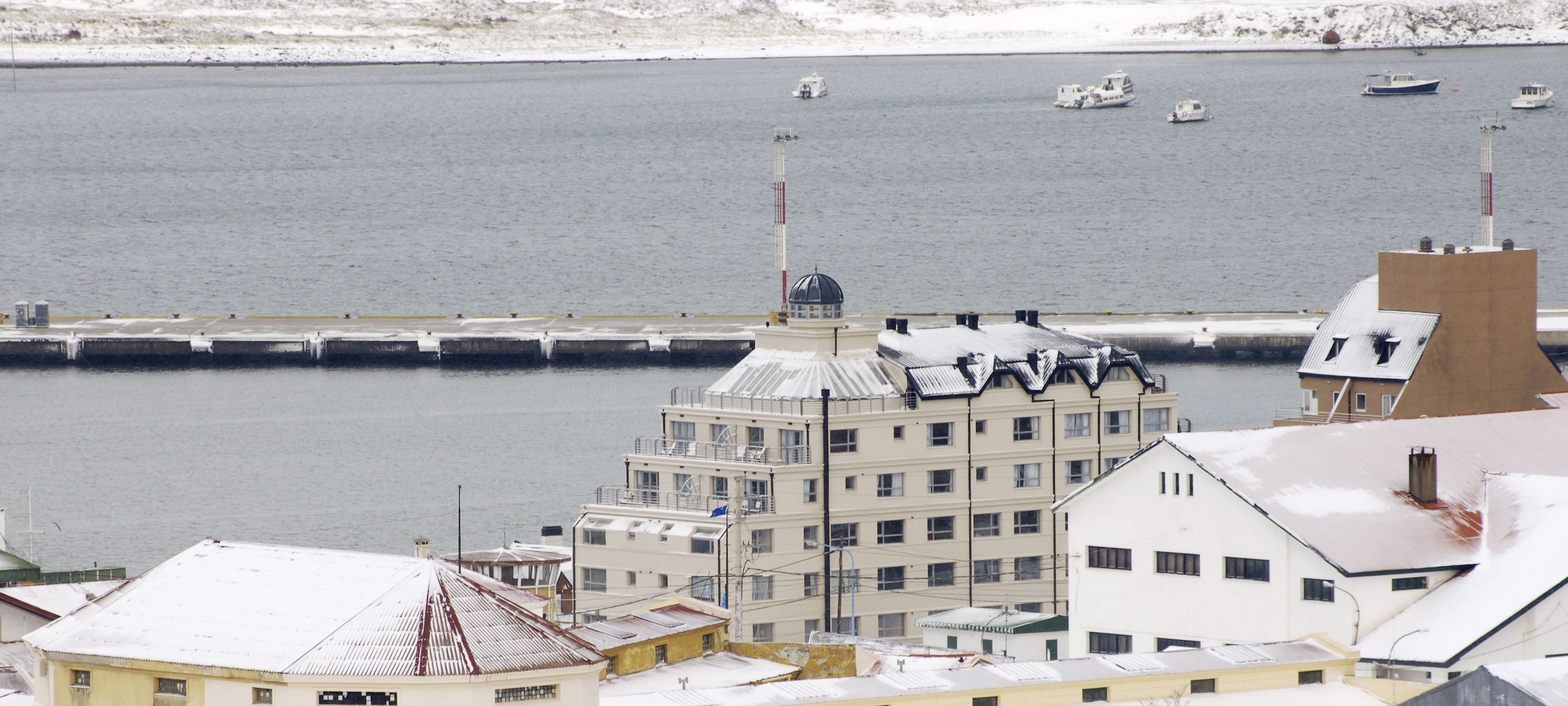 Um edifício costeiro com vários andares, uma torre imponente e um cais com barcos.