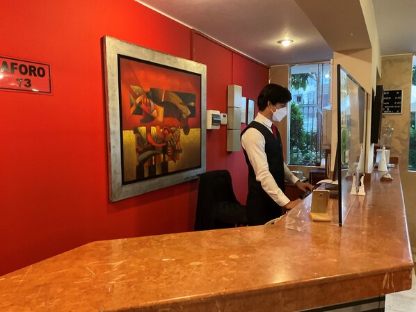 Uma área de recepção de hotel com balcão de mármore, uma pintura abstrata emoldurada e uma placa indicando a sala 73.