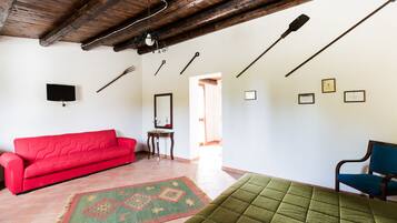 Quarto com sofá vermelho, um banquinho verde, uma cadeira azul e teto de madeira com vigas aparentes.