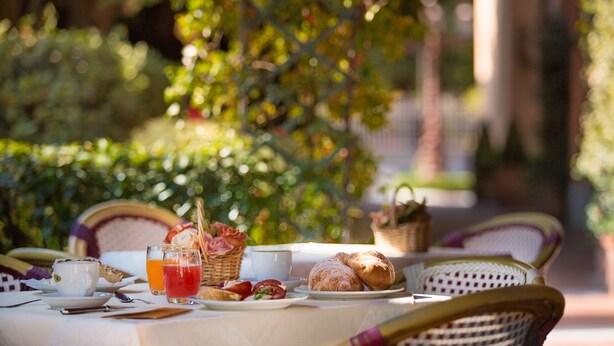 Mesa posta ao ar livre com itens de café da manhã, incluindo pão, uma xícara e um copo de suco.
