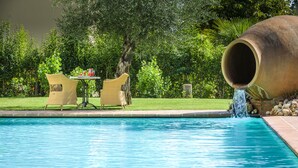 Piscina com um elemento aquático, cercada por vegetação e uma mesa com cadeiras.