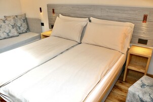 Quarto de hotel moderno com uma cama grande, duas mesinhas de cabeceira e um pequeno sofá.