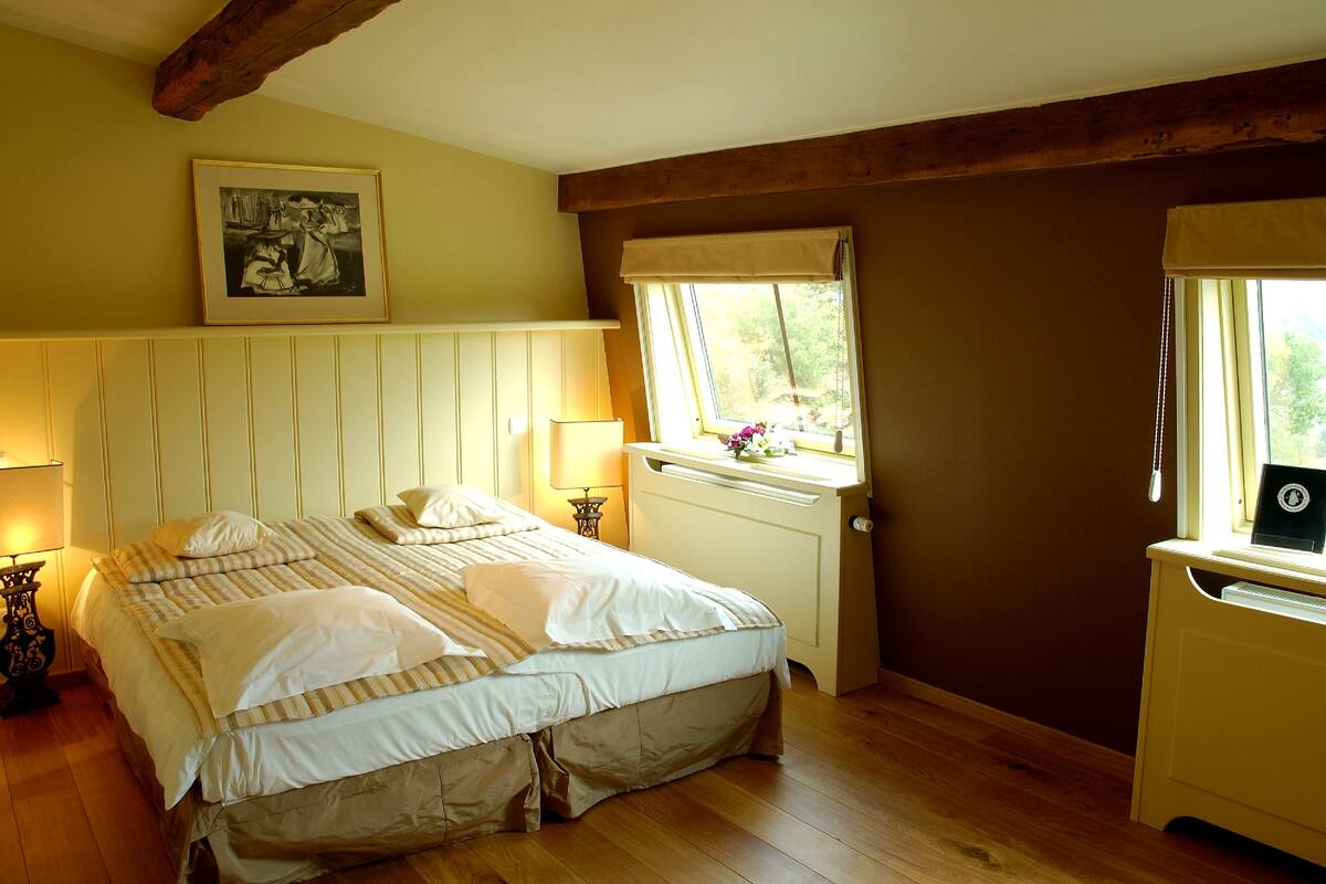 Quarto com cama, luminárias de cabeceira, janela com vista e radiador.