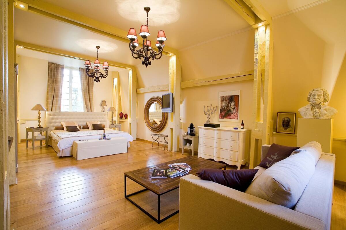 Quarto amplo e bem iluminado, com uma cama grande, um sofá, uma mesa de centro e um candelabro.