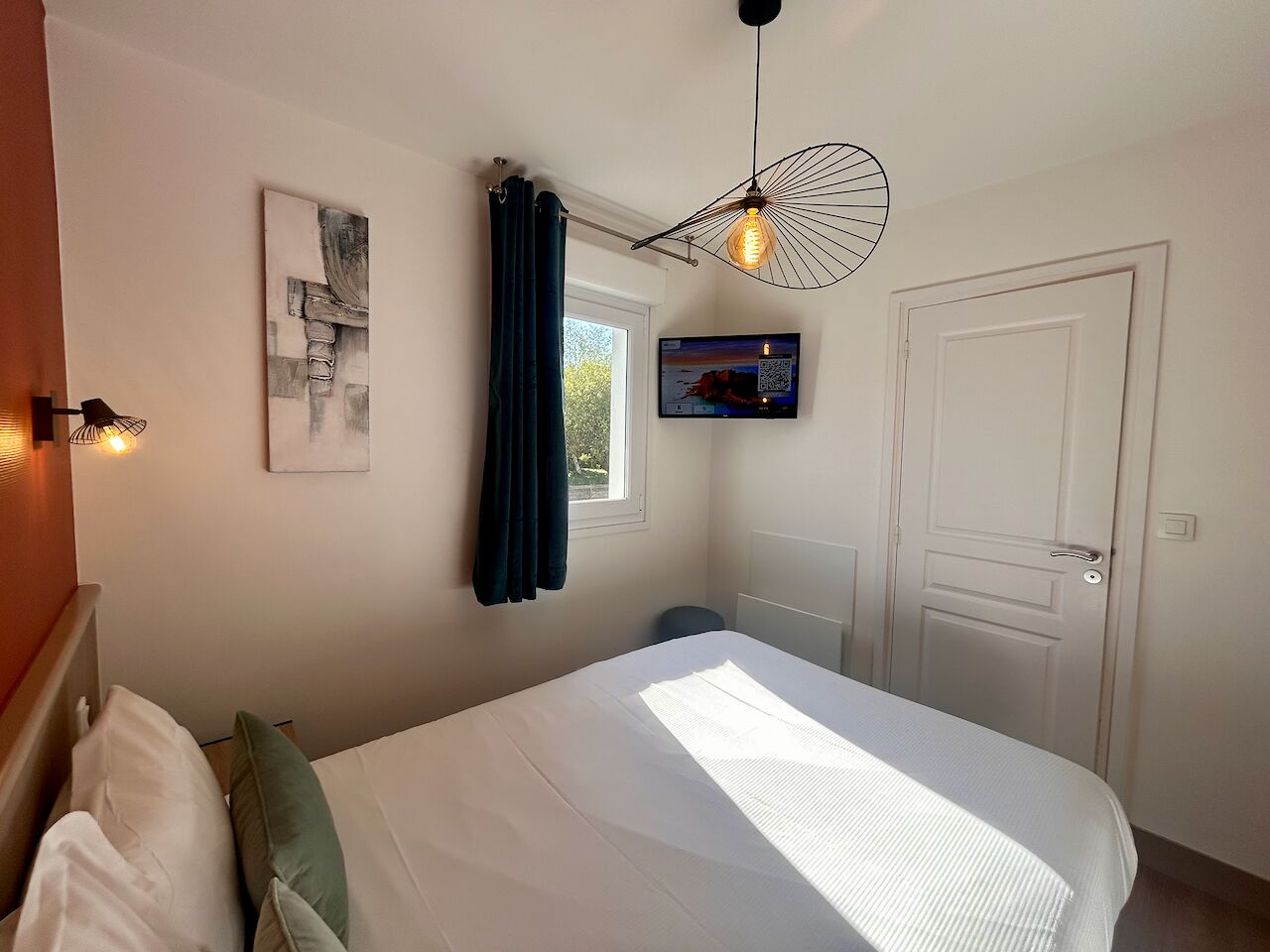 Quarto com cama, quadro, televisão, janela com cortinas e porta.
