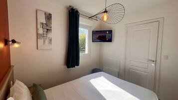 Quarto com cama, quadro, televisão, janela com cortinas e porta.