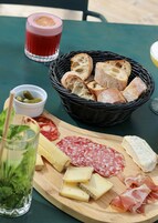 Uma tábua de madeira com diversos queijos, salame e pão sobre uma mesa.