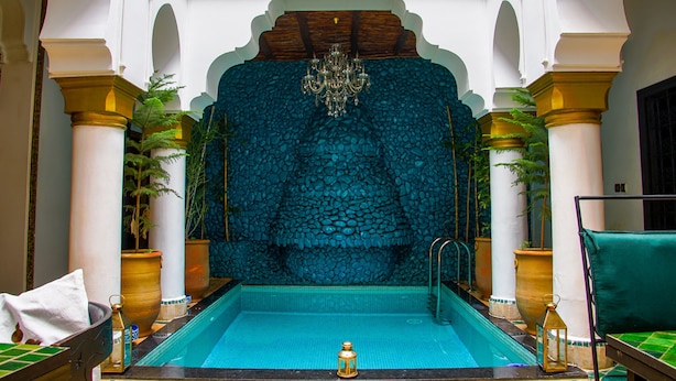 Piscina com parede decorativa, rodeada por colunas e plantas em vasos.
