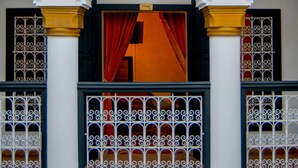 Fachada de edifício com janelas arqueadas, grades metálicas decorativas e um lampião pendurado.