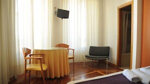 Quarto de hotel com cama, mesa redonda com cadeiras, televisão e porta para um banheiro.