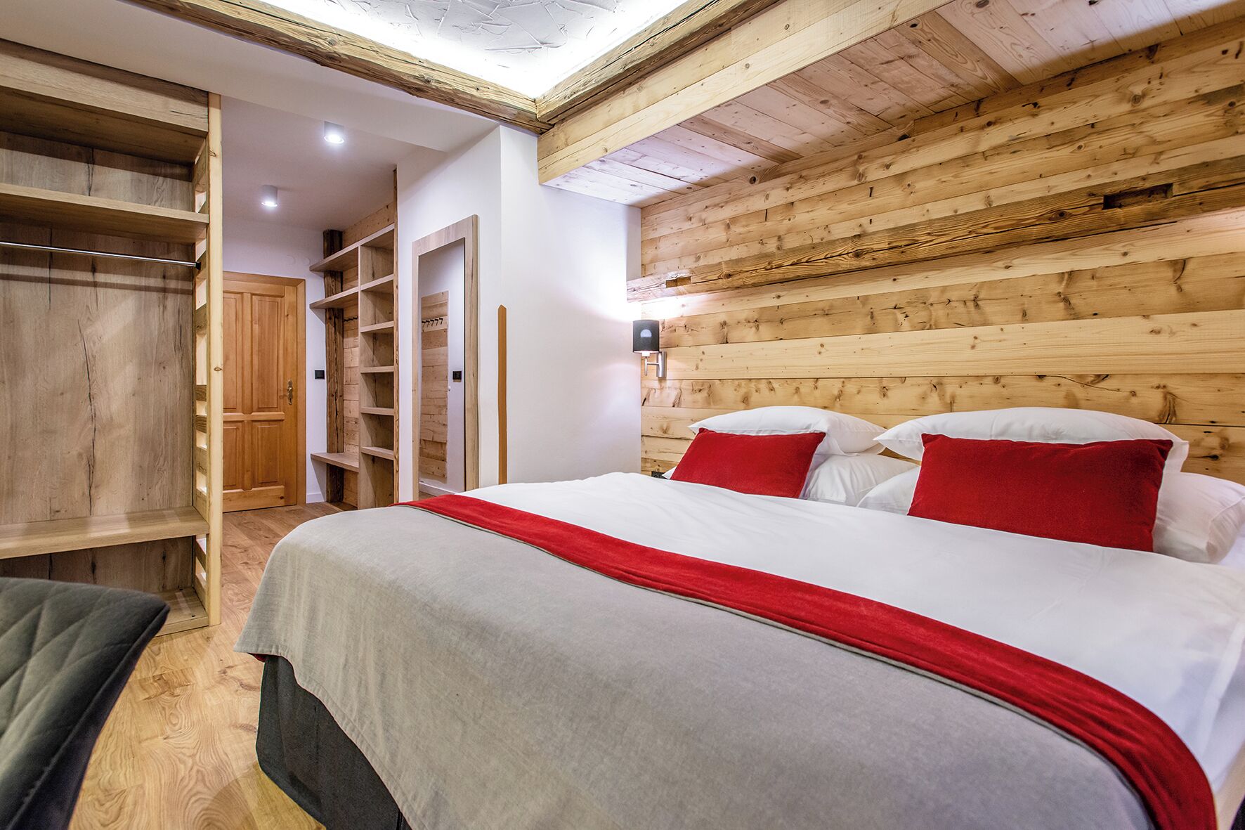 Quarto com cabeceira de madeira, cama com roupa de cama branca e vermelha, e guarda-roupa embutido.