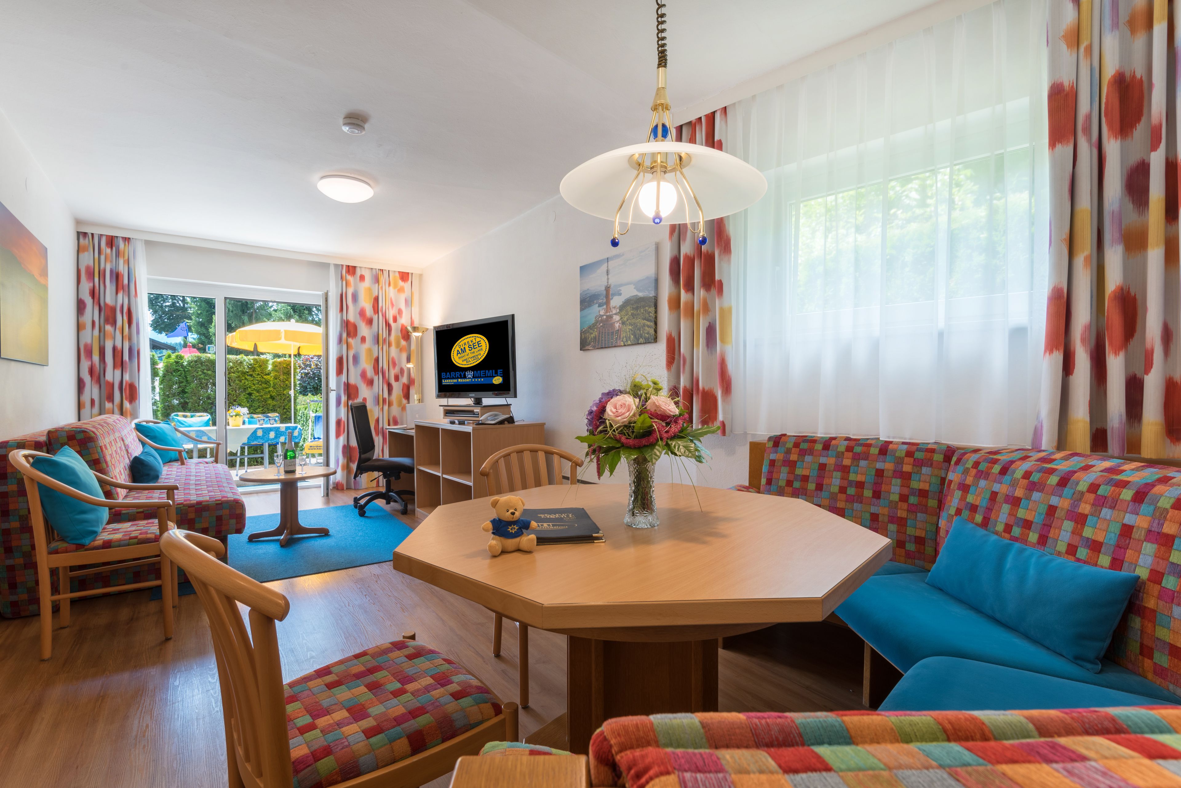Uma sala de estar aconchegante com uma mesa de jantar de madeira, sofás coloridos e uma televisão.