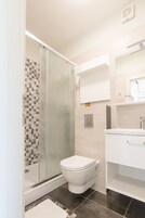 Um banheiro moderno com box de vidro, vaso sanitário e pia com espelho acima.