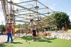 Um percurso de obstáculos ao ar livre com uma ponte de corda e um putting green.
